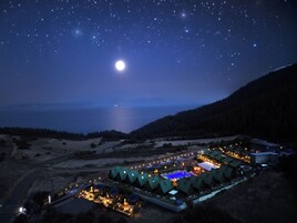 Um resort com várias cabanas em formato de cúpula, uma piscina e vista para o oceano sob um céu estrelado.