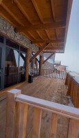 Um deck de madeira com paredes de pedra, uma porta de vidro e um corrimão de madeira.