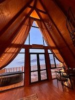 Um quarto acolhedor, em formato triangular, com janelas amplas que exibem uma vista de uma paisagem nevada.