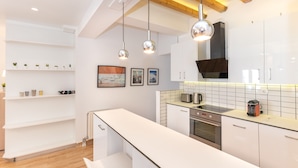 Uma cozinha moderna com armários brancos, teto de madeira, luminárias pendentes e painel de azulejos.