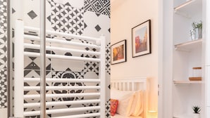 Um banheiro moderno com azulejos estampados, um radiador branco, uma cama com cabeceira branca e uma prateleira com plantas.