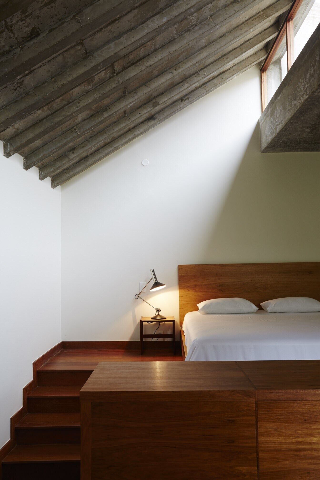 Quarto com cabeceira de madeira, mesa de cabeceira com abajur e cama com roupa de cama branca.