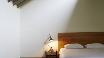 Quarto com cabeceira de madeira, mesa de cabeceira com abajur e cama com roupa de cama branca.