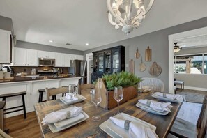 Cozinha moderna com armários brancos, uma mesa de jantar de madeira para quatro pessoas e um candelabro.