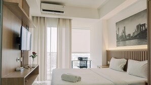 Quarto de hotel com cama, televisão fixada na parede, janela com cortinas e pintura de paisagem urbana na parede.