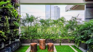 Jardim no terraço com grama sintética, vasos de madeira e diversas plantas verdes.
