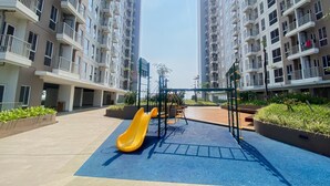 Um parquinho com um escorrega amarelo e equipamentos de exercício numa área residencial urbana com edifícios altos.
