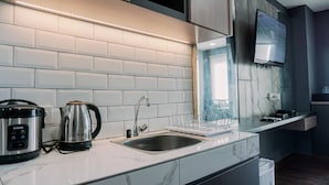 Uma cozinha moderna com azulejos brancos tipo metrô, uma pia de aço inoxidável, chaleira e cozedor de arroz.
