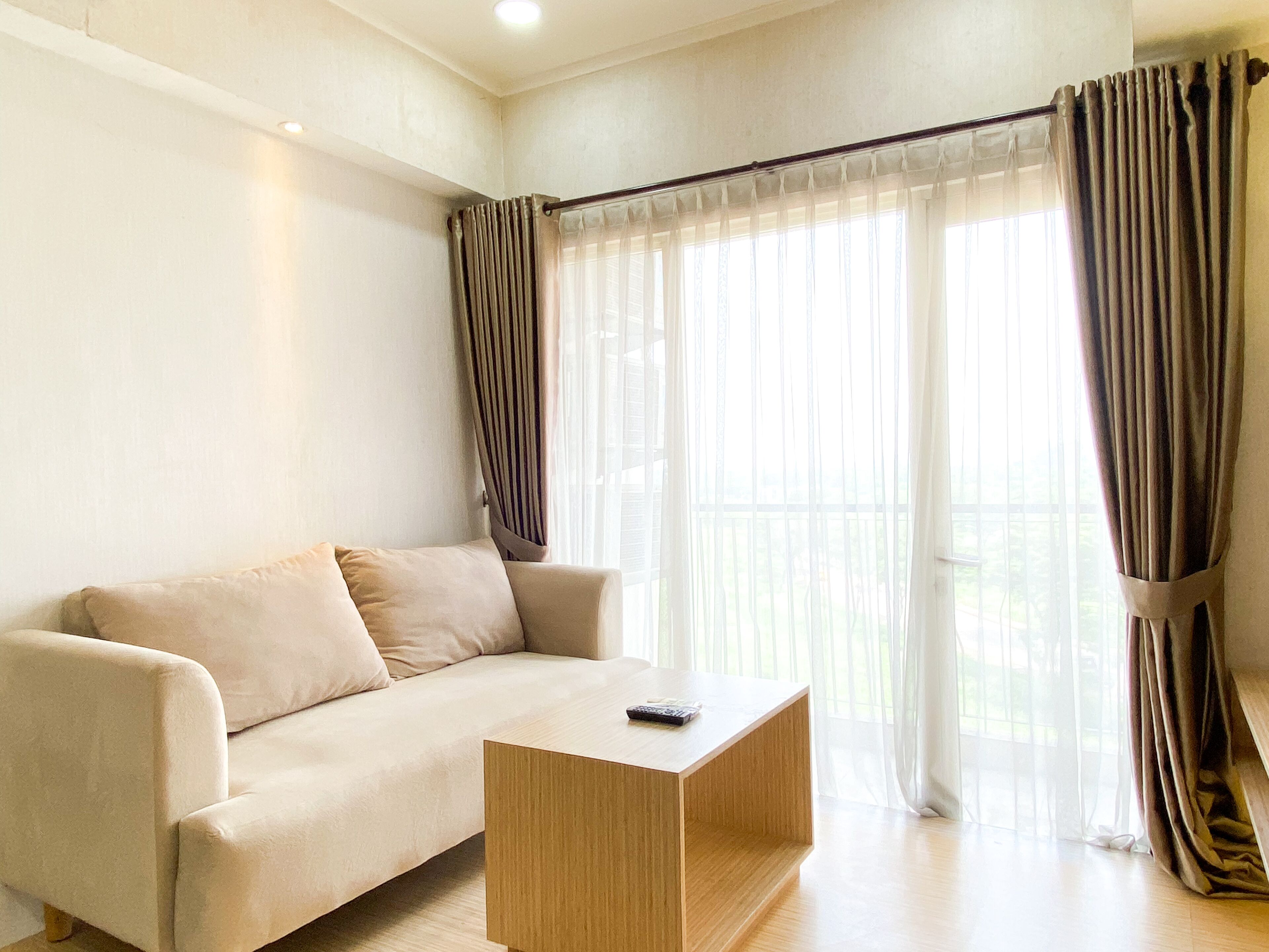Uma sala de estar moderna com um sofá bege, uma mesa de centro de madeira e cortinas leves numa grande janela.
