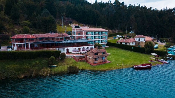 Um edifício grande, de vários andares, com telhado de telhas vermelhas, localizado à beira de um lago.