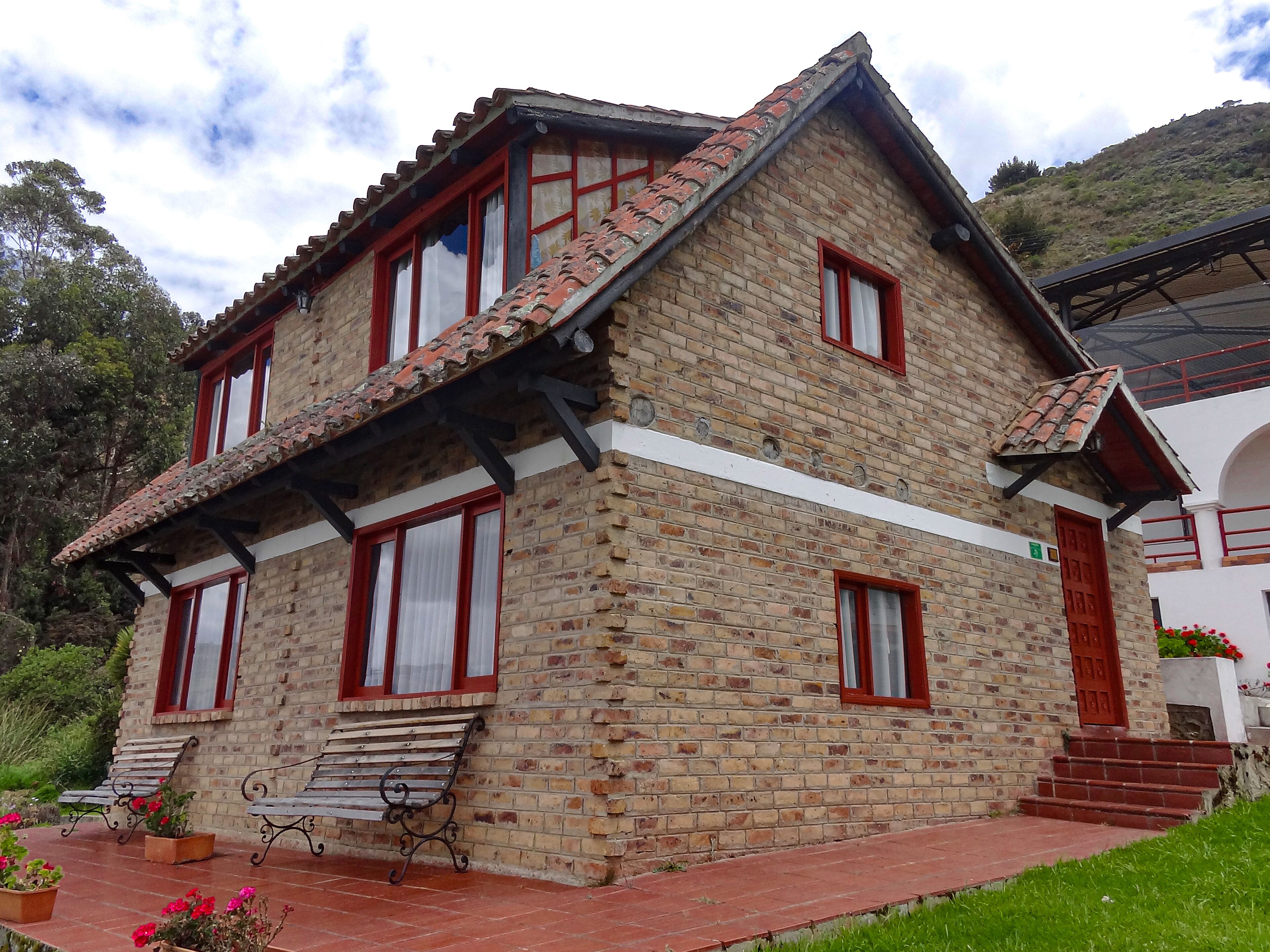 Uma casa de pedra de dois andares com janelas emolduradas em vermelho, um banco de madeira e um caminho de tijolos vermelhos que leva à entrada.