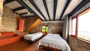 Um quarto com teto inclinado, paredes de tijolo, chão de madeira, duas camas, um sofá vermelho e uma janela com vista.
