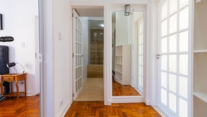 Um corredor com piso de madeira, paredes brancas e porta de armário espelhada.