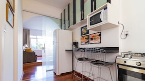Cozinha compacta com micro-ondas, fogão a gás e dois banquetas.