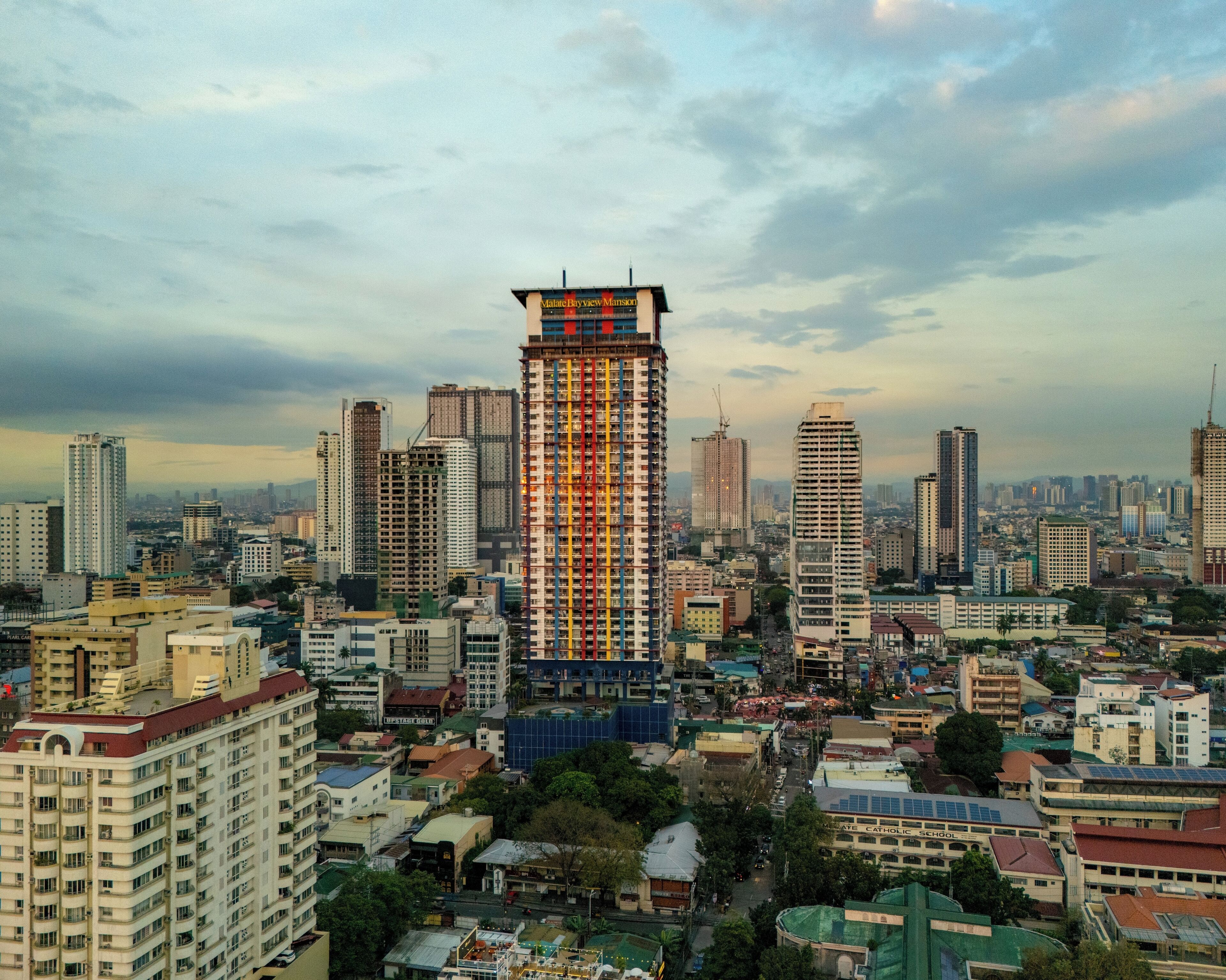 Um edifício alto com fachada listrada característica, rodeado por um ambiente urbano denso com outros edifícios e céu claro.