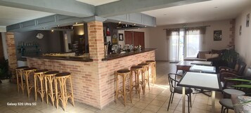 Uma área de bar moderna com balcão de tijolos, vários bancos e um espaço de estar com mesas e cadeiras.