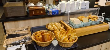 Um buffet de café da manhã com pães, doces e uma estação de café.