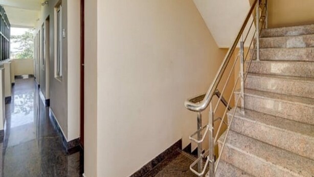 Um corredor com escada que leva a um andar superior, com corrimão e guarda-corpo de metal.