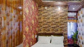 Quarto de hotel com cabeceira de madeira, cama com roupa branca, parede estampada e janela com cortinas.