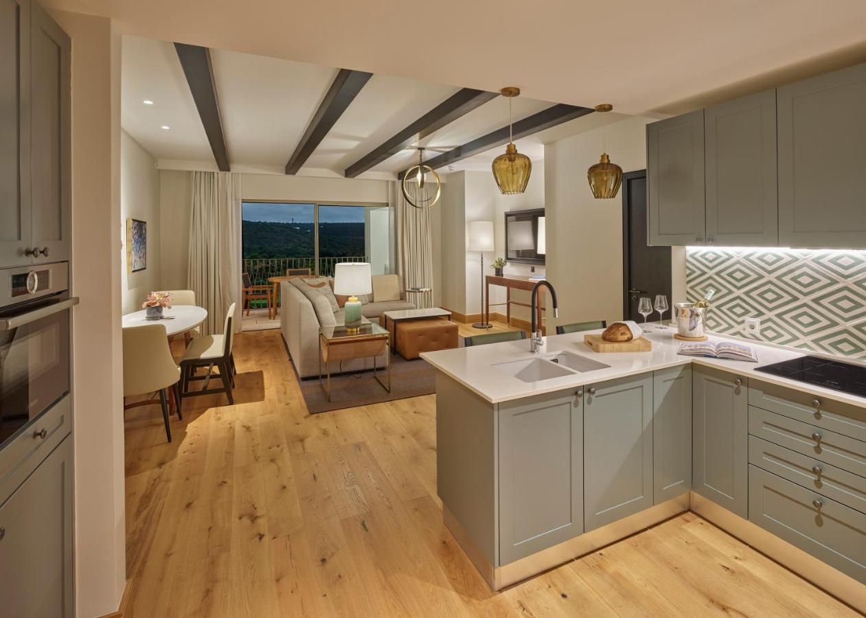 Uma cozinha moderna com armários cinza, uma ilha central e uma área de refeições com vista para o exterior.