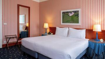 Quarto de hotel com uma cama grande, duas mesas de cabeceira com abajures, uma cadeira e um quadro na parede.