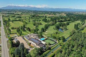 Vista aérea de um campo de golfe com um edifício de hotel que inclui painéis solares, quadra de tênis e estacionamento.