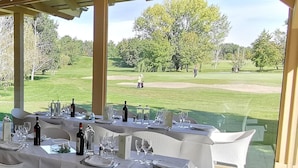 Uma área de refeições ao ar livre com mesas preparadas para uma refeição, com vista para um campo de golfe.
