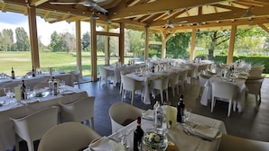 Restaurante ao ar livre com mesas preparadas para refeições, com vista para um campo de golfe.