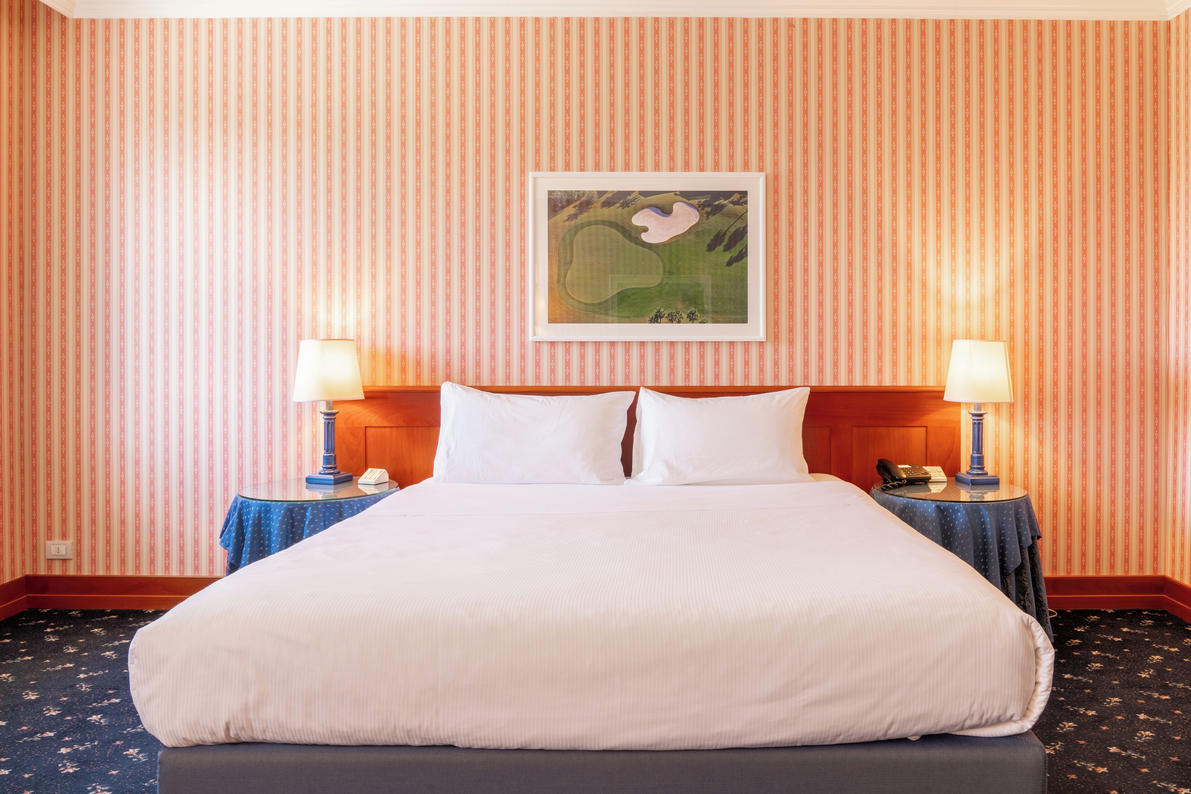 Quarto de hotel com uma cama grande, papel de parede listrado e um quadro na parede.