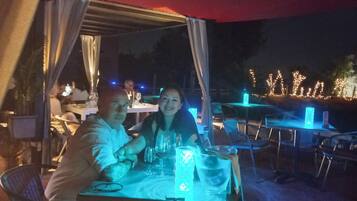 Um casal jantando em uma mesa ao ar livre sob um toldo vermelho.
