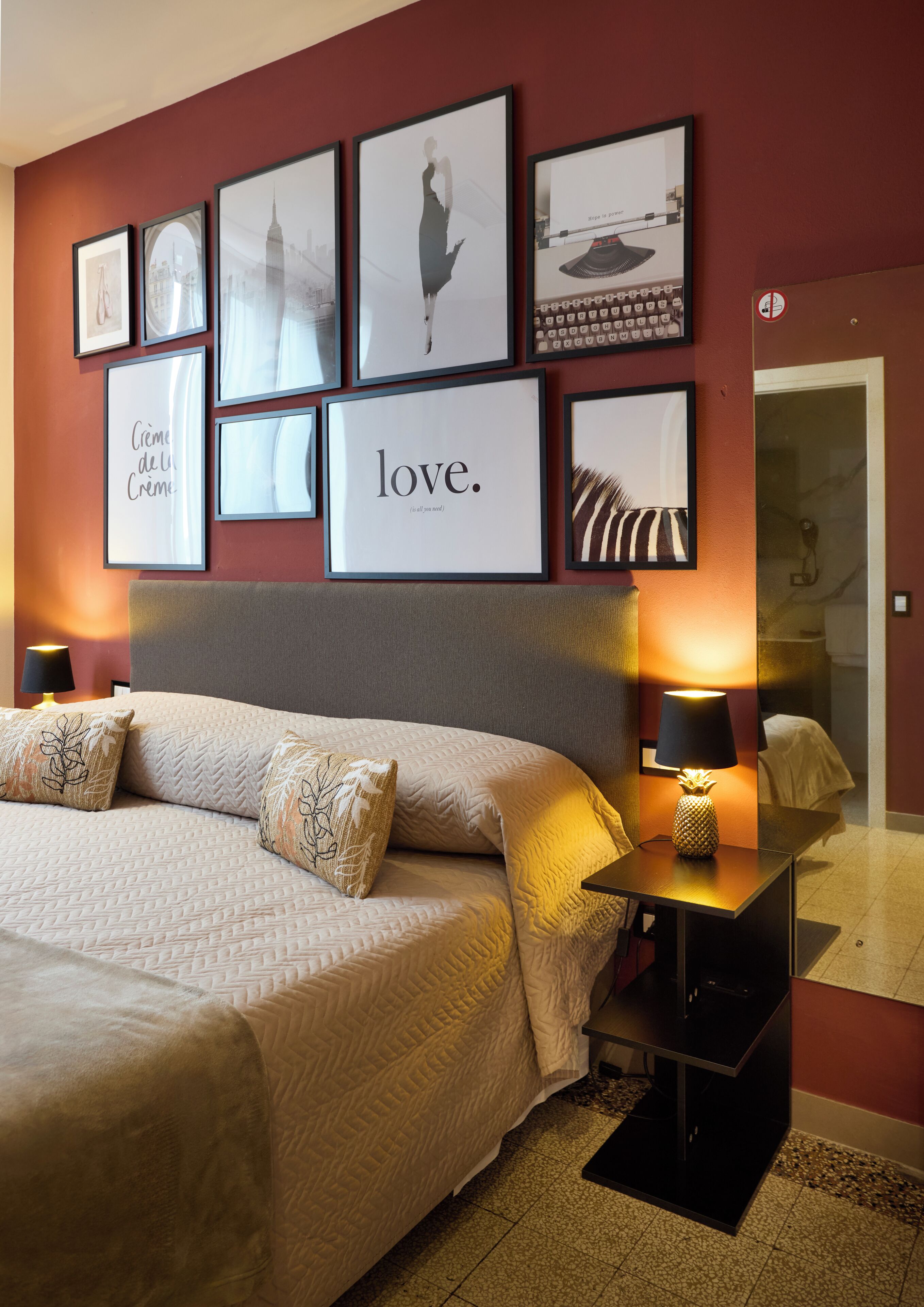 Quarto de hotel com uma cama grande, duas mesas de cabeceira com luminárias, um encosto de cama e uma parede decorada com quadros.