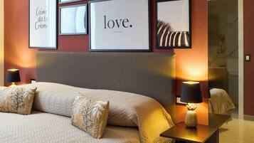 Quarto de hotel com uma cama grande, duas mesas de cabeceira com luminárias, um encosto de cama e uma parede decorada com quadros.