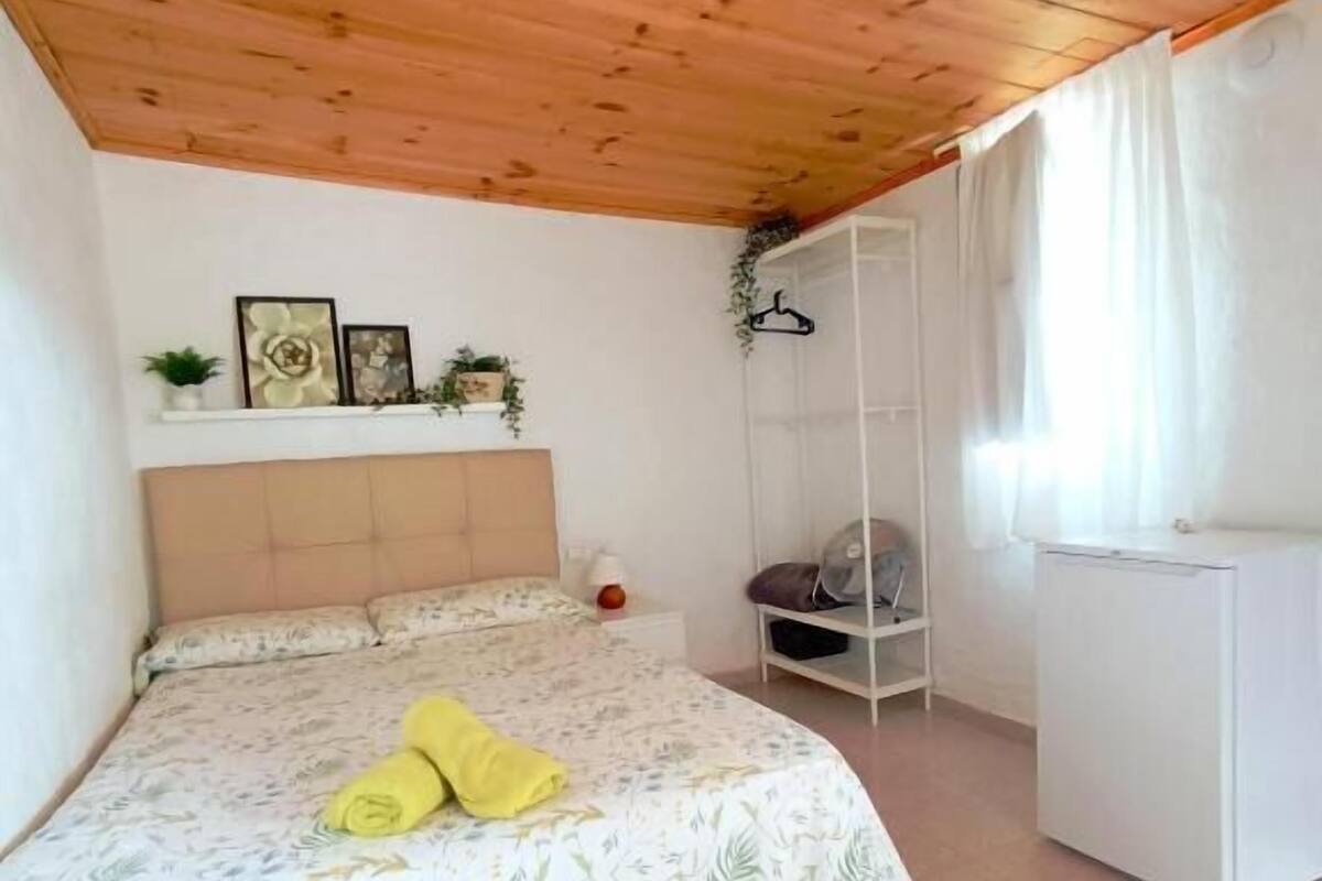 Quarto com cama, guarda-roupa, uma mesinha e uma planta pendente.