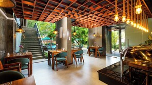 Restaurante com mesas e cadeiras de madeira, um lance de escada e luminárias pendentes.