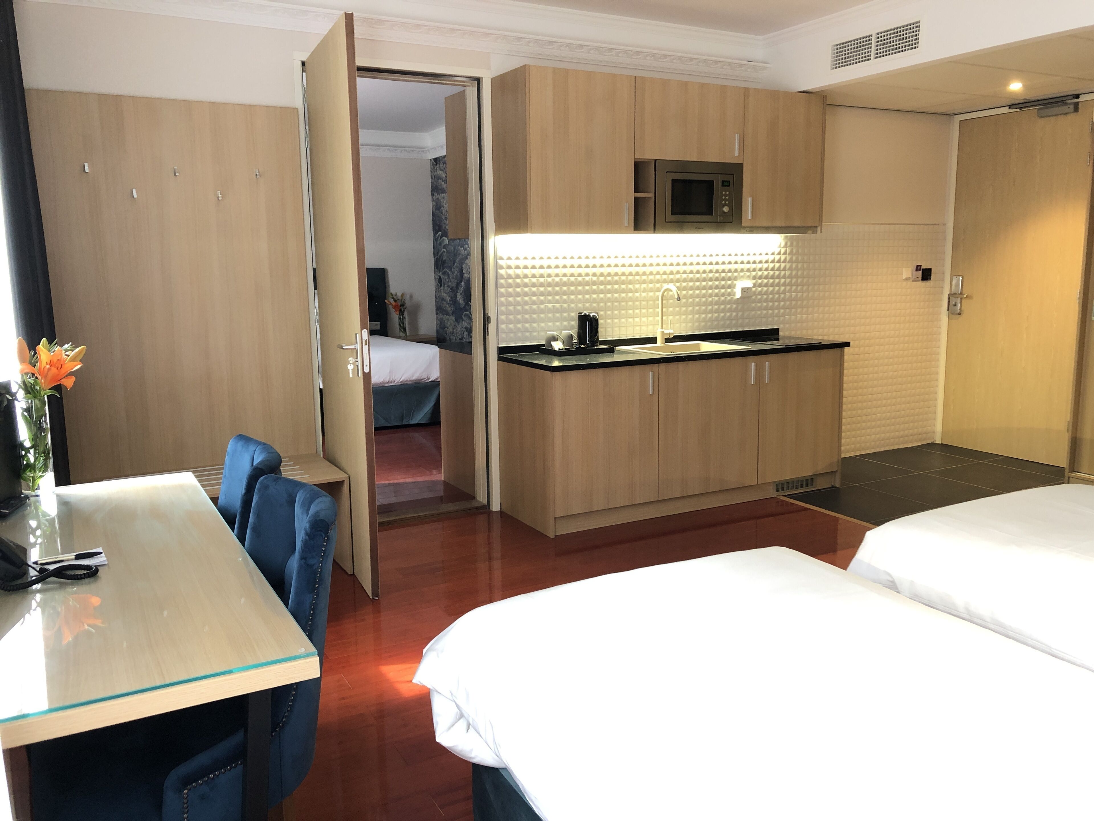 Quarto de hotel com cama, escrivaninha e cadeira, cozinha compacta com micro-ondas e banheiro.