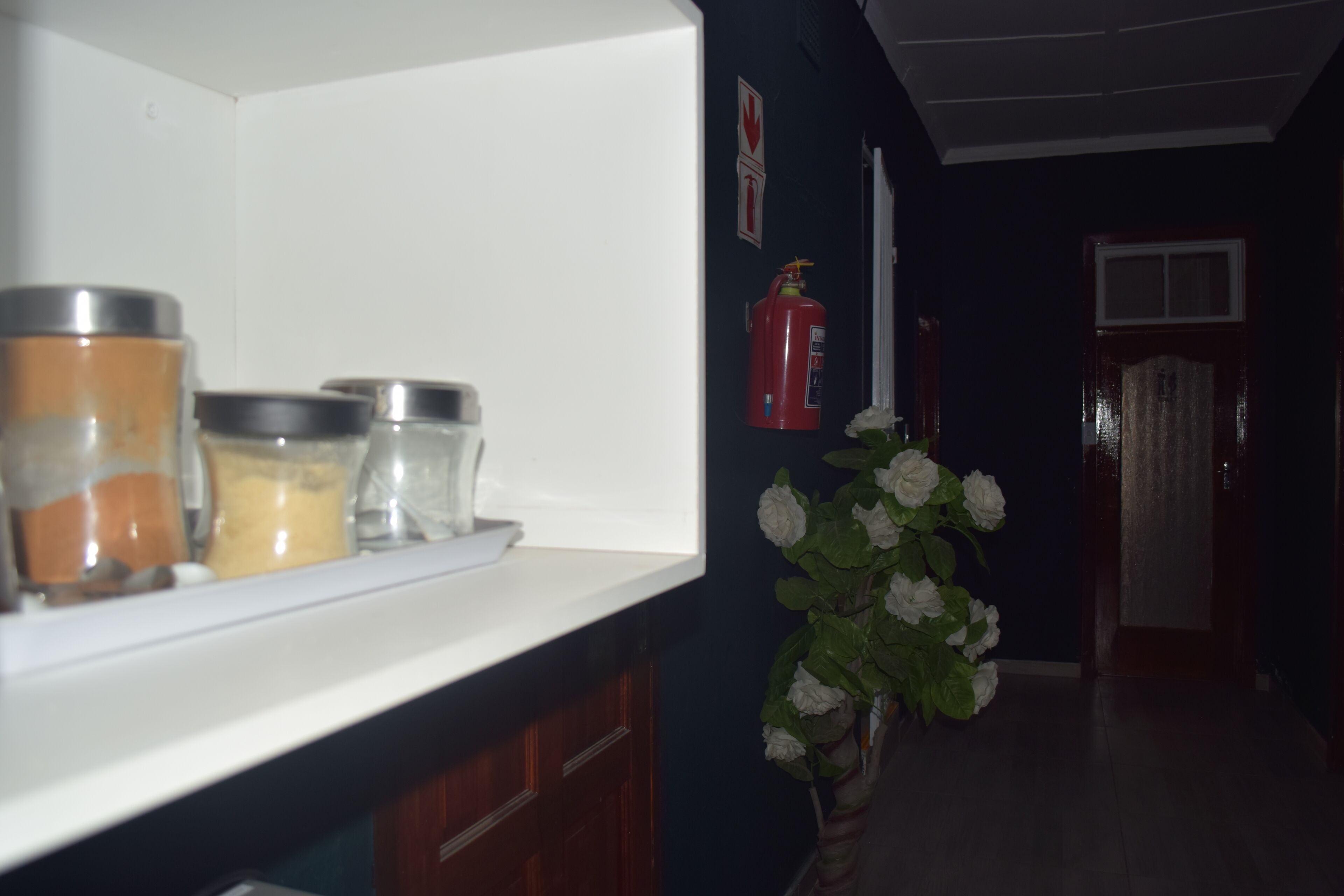 Uma cozinha com bancada branca, potes e um vaso com flores brancas.