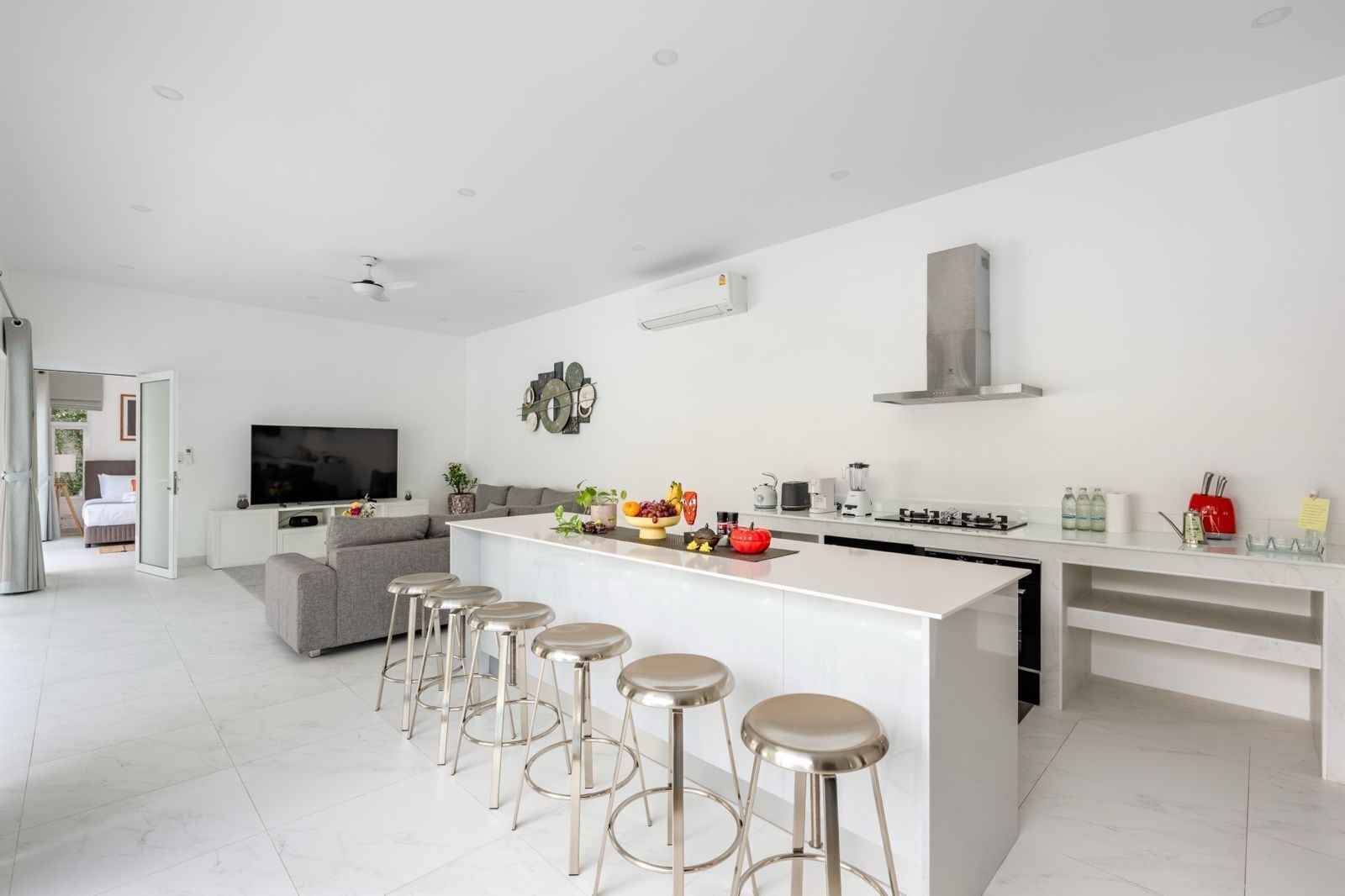 Cozinha moderna com uma ilha central, banquetas de bar, área de jantar e sala de estar com sofá e televisão.