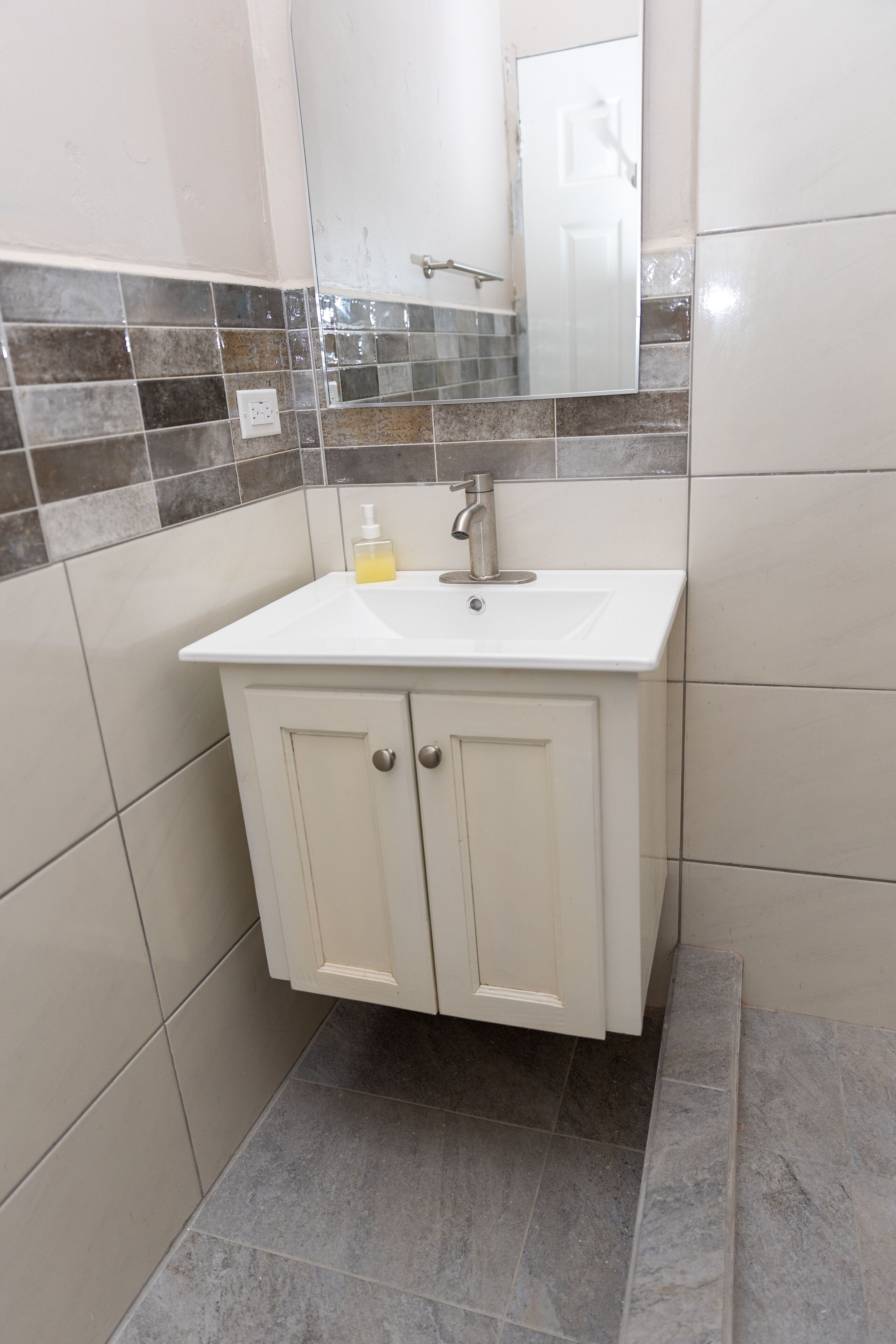 Casa de banho com lavatório branco, espelho e painel de azulejos.