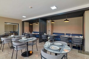 Um restaurante moderno com mesas redondas, cadeiras estofadas cinzas e iluminação pendente.