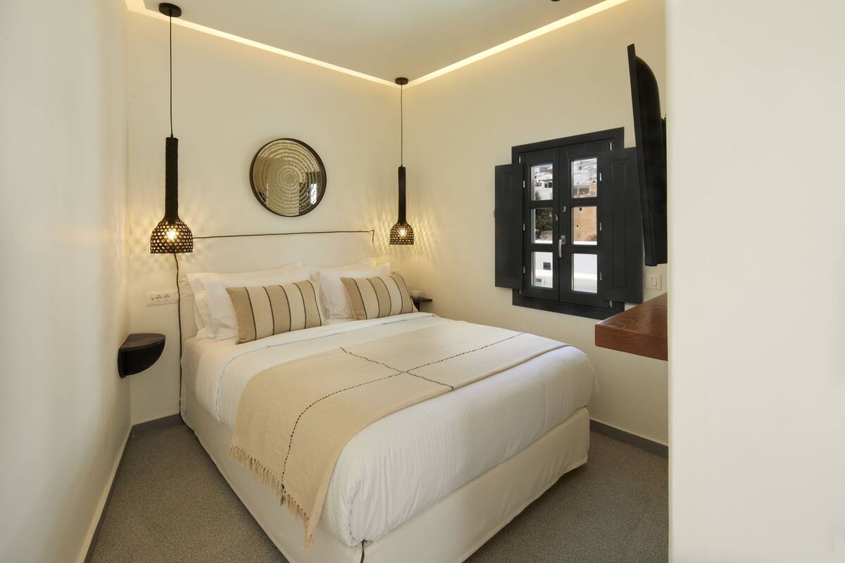 Quarto bem arrumado com uma cama grande, duas luminárias de parede, um espelho e uma janela com persianas.