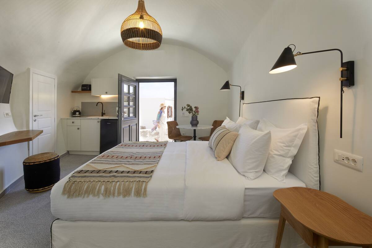 Quarto com uma cama grande, mesa de cabeceira, abajur e vista para a cozinha e varanda.