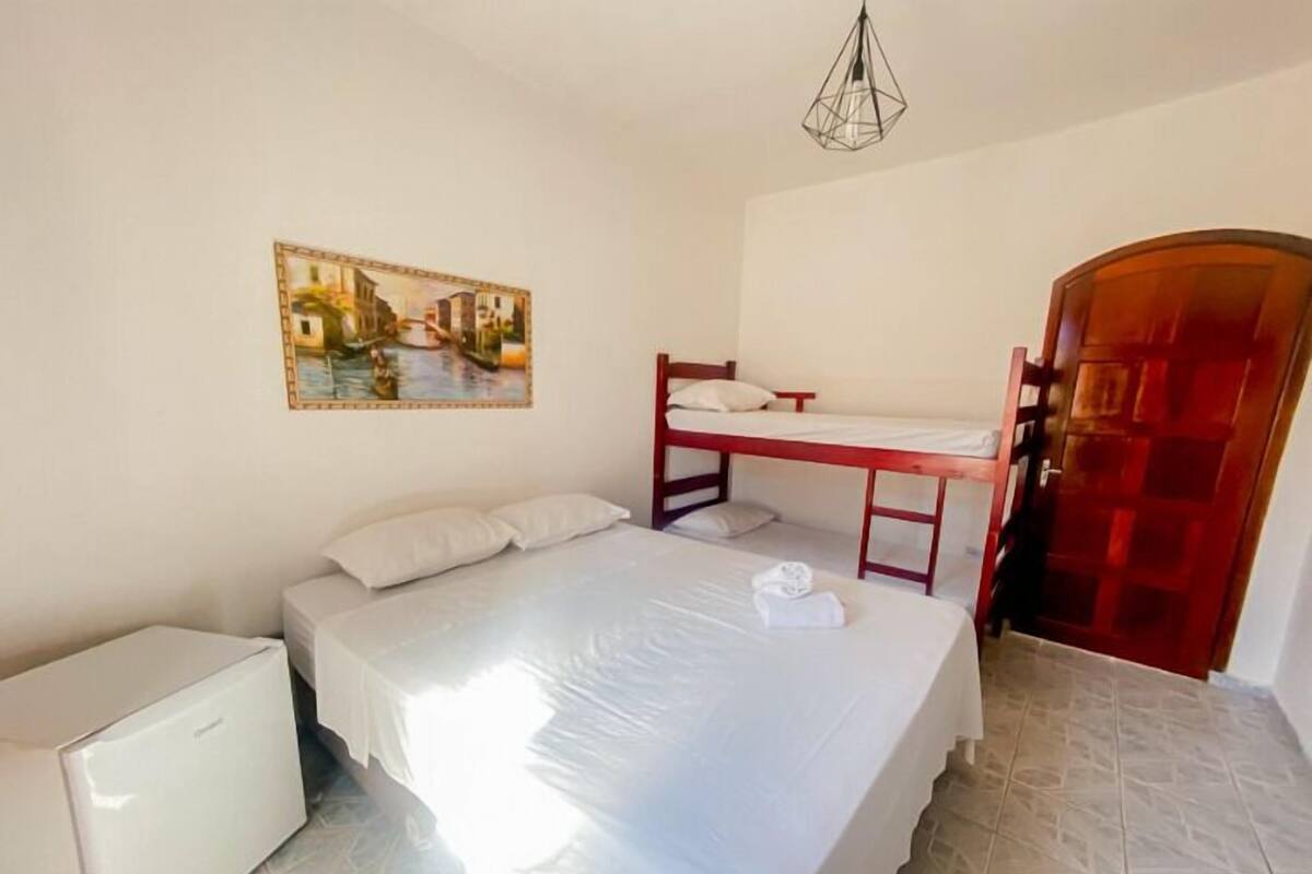 Quarto com uma cama de solteiro, uma pequena escrivaninha, uma cadeira, um guarda-roupa e uma porta.