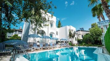 Piscina com espreguiçadeiras e guarda-sóis, um edifício branco com janelas em arco e uma placa para KemerRoyce Beach Hotel.
