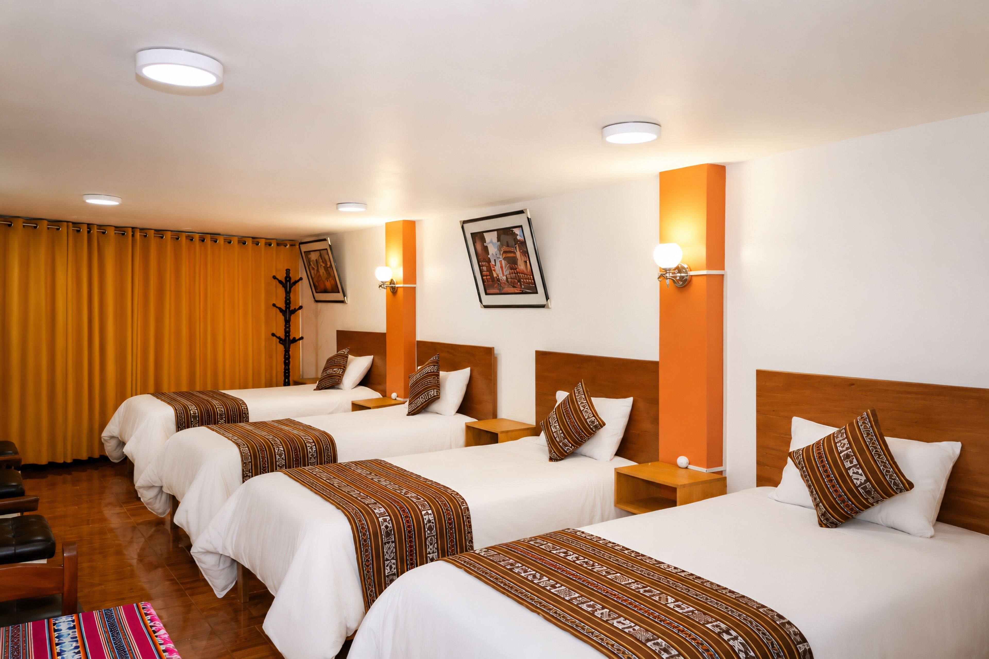 Quarto de hotel com quatro camas, cada uma com colcha e almofadas estampadas, cabeceira de madeira e mesa de cabeceira.