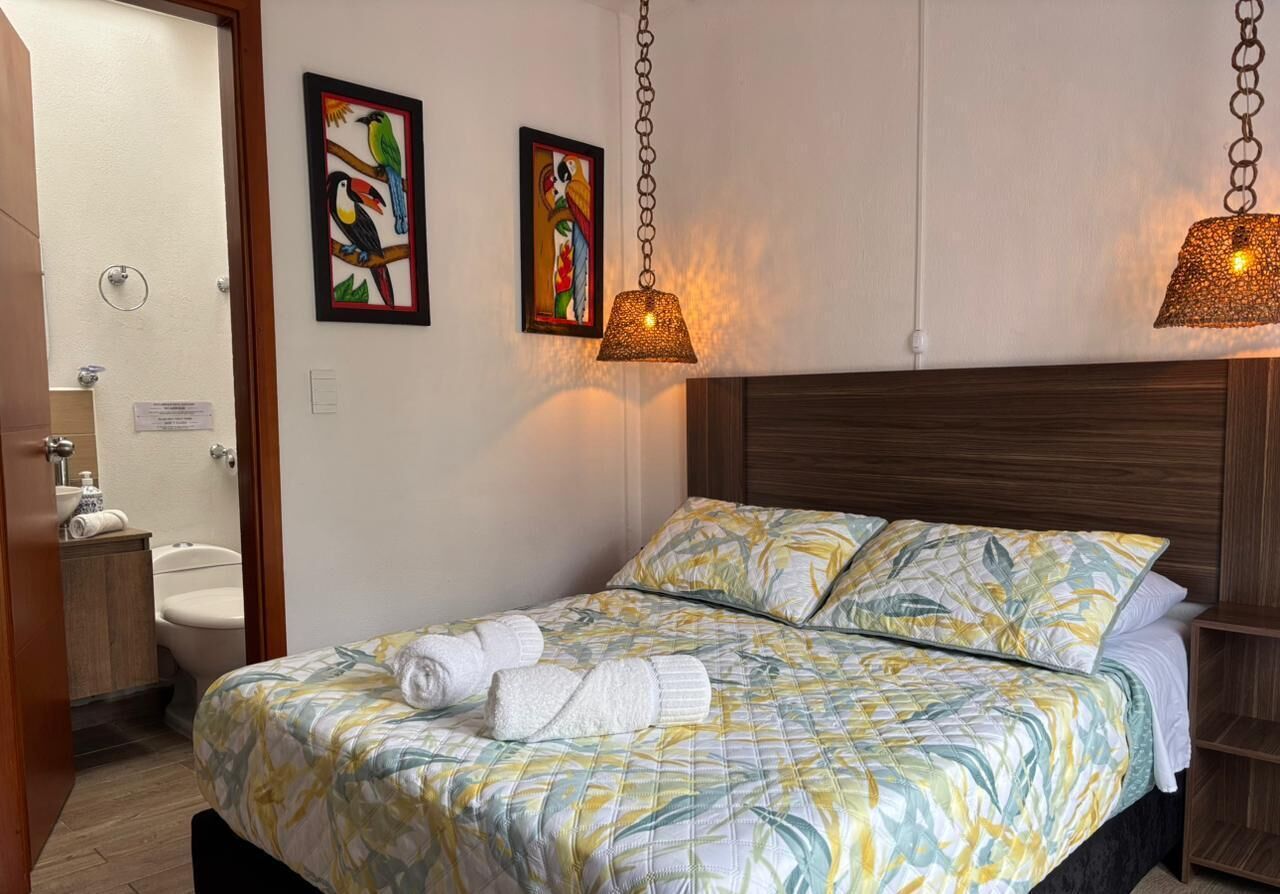 Quarto de hotel com uma cama, duas luminárias fixadas na parede e duas obras de arte emolduradas.