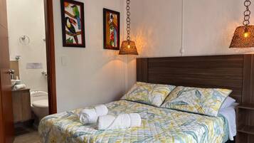 Quarto de hotel com uma cama, duas luminárias fixadas na parede e duas obras de arte emolduradas.