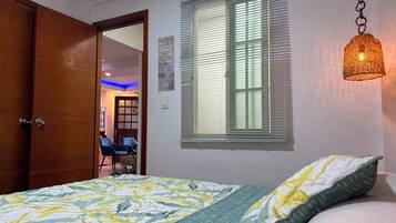Um quarto com cama, janela com persianas, luminária pendente e porta.