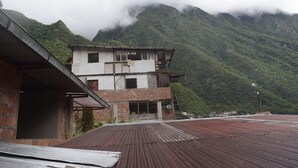 Um edifício de vários andares com telhado de metal corrugado, rodeado por montanhas verdejantes e névoa.