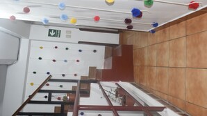 Um quarto com piso de madeira, teto branco com pompons coloridos, sinal de saída visível e uma escada.