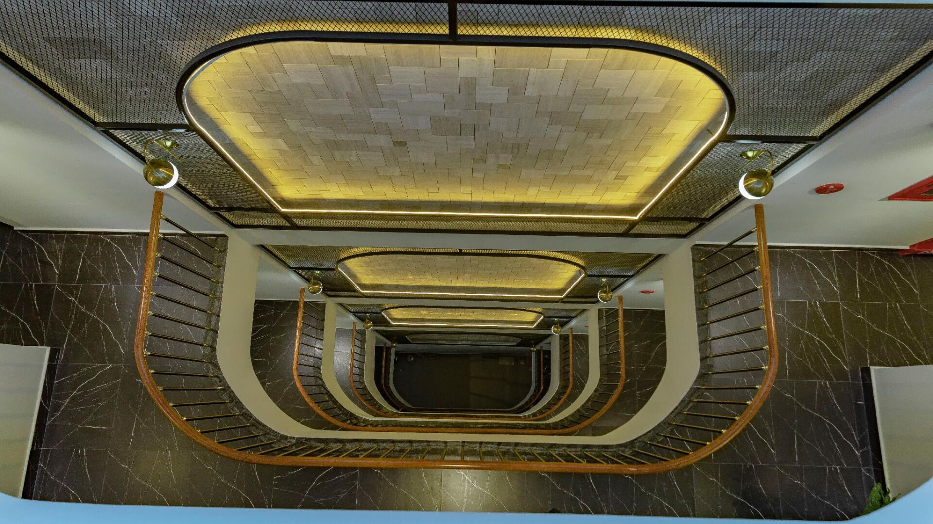 Uma escadaria em espiral com design moderno, destacando teto trabalhado e paredes com textura semelhante a mármore.